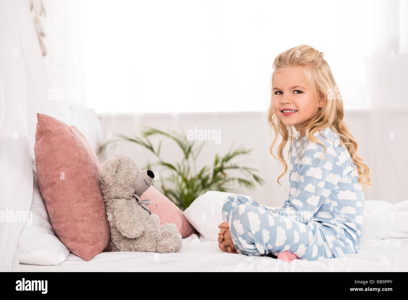 cute child sitting on bed with crossed legs and teddy bear Stock Photo ...