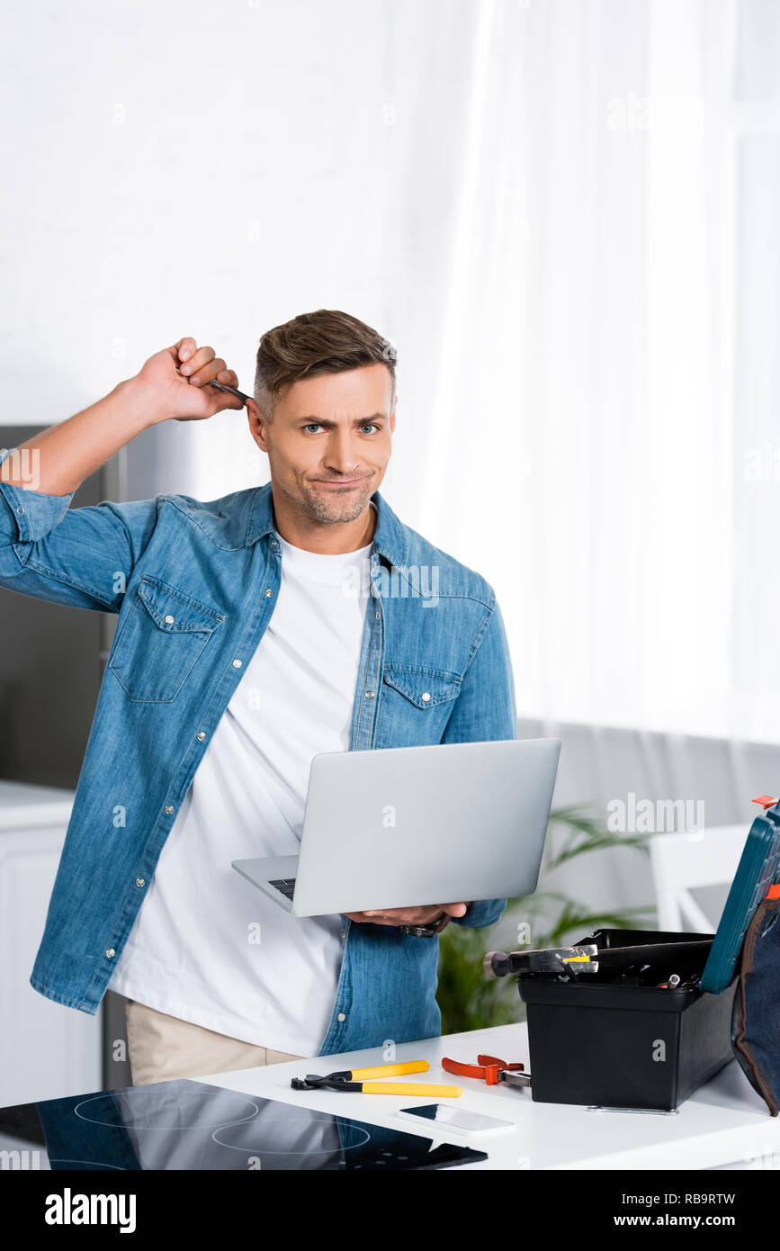 confused man holding laptop and scratching head with tool Stock Photo ...