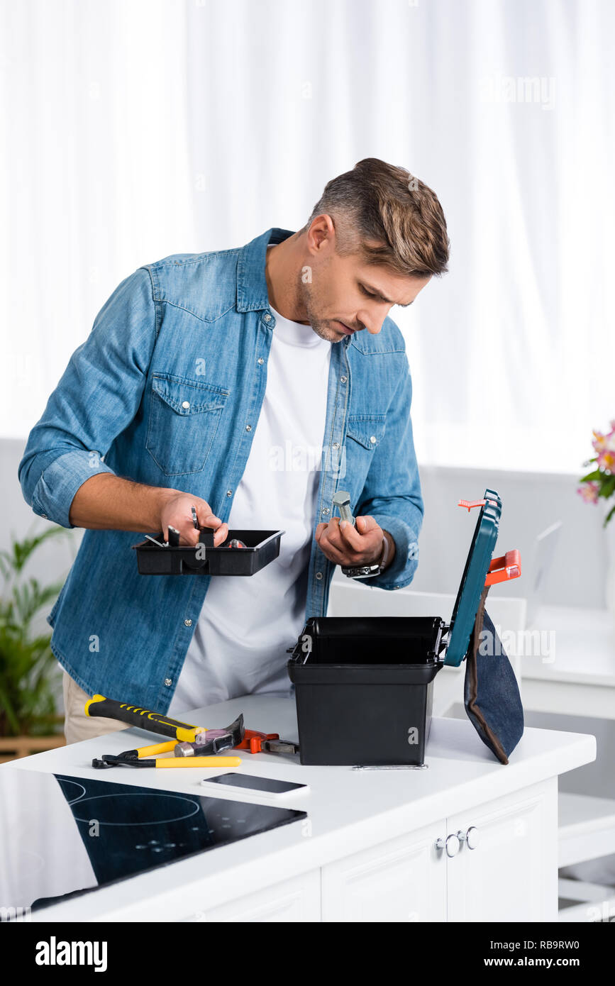 handsome man looking inside tool box while standing in kitchen Stock ...