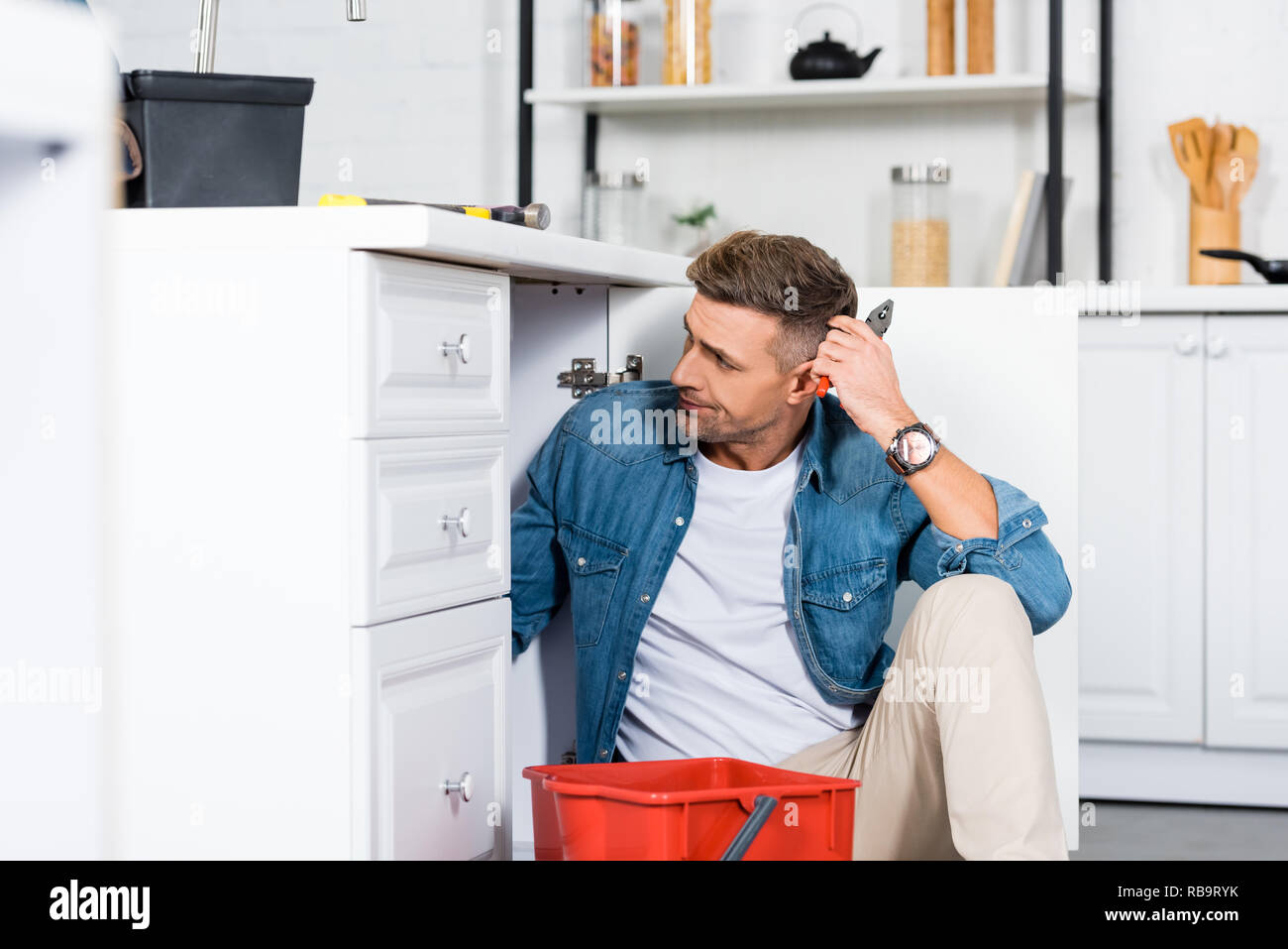 confused man sitting on floor while repairing kitchen sink Stock Photo ...
