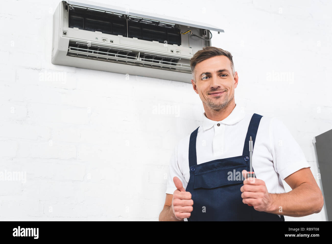 handsome repairman showing thumb up gesture with air conditioner at ...