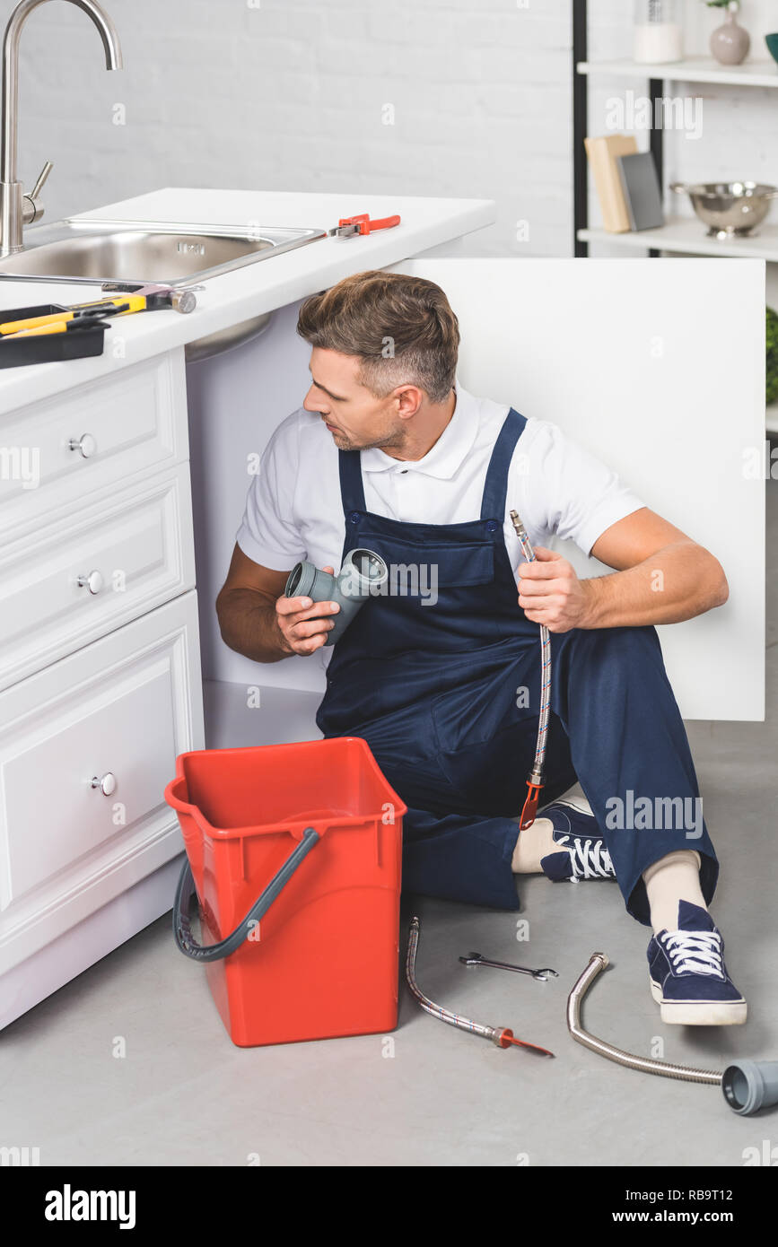 adult repairman with red plastic bucket holding pipes for repairing kitchen sink Stock Photo - Alamy
