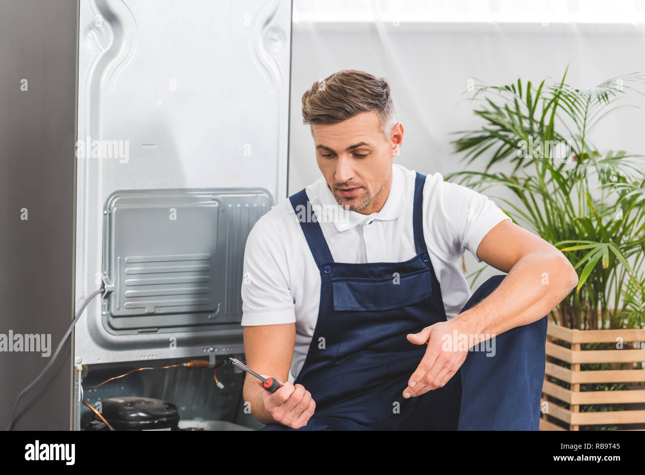 confused adult repairman looking at screwdriver while repairing ...