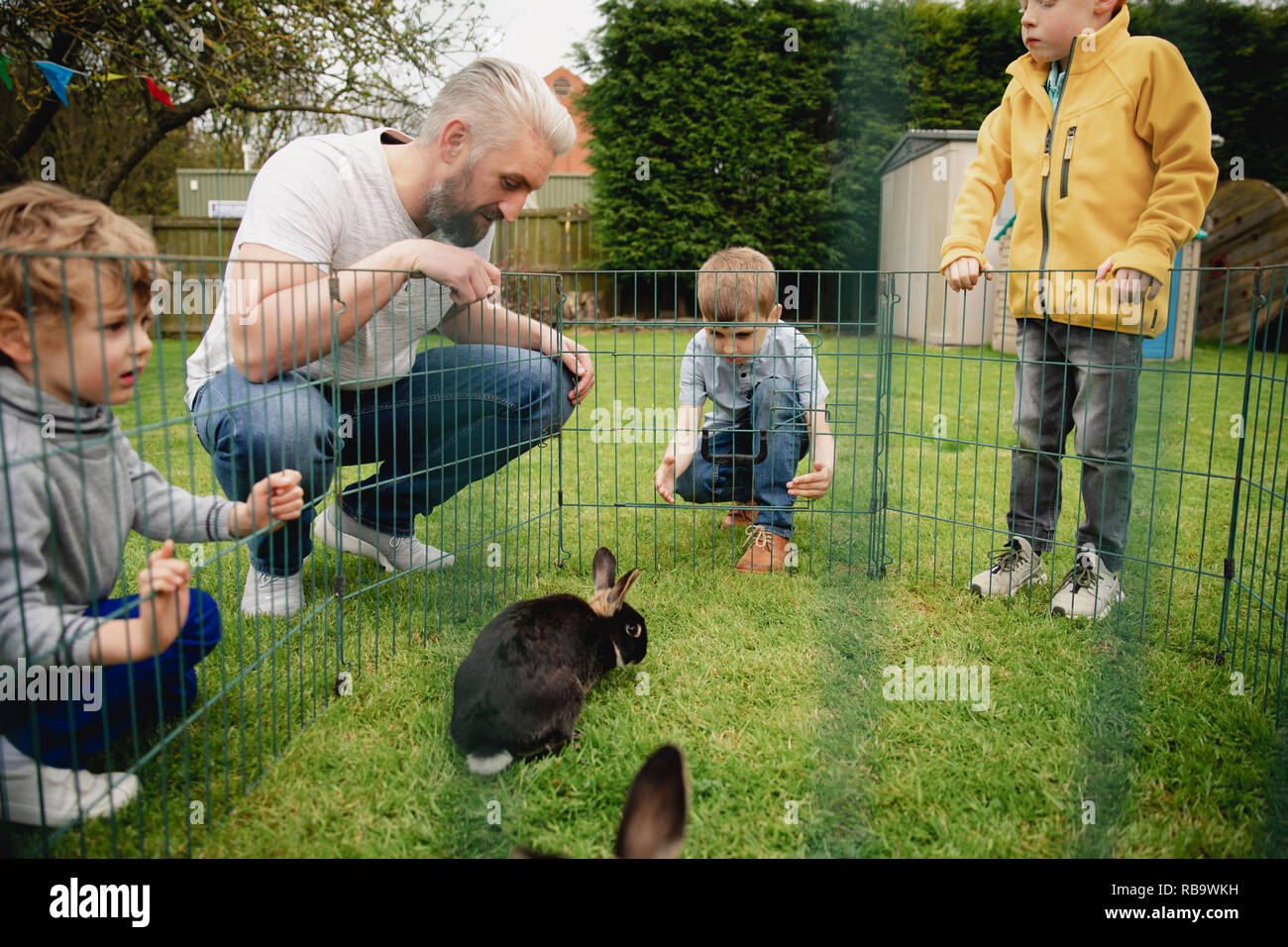 Group of children kneeling outdoors next to a rabbit pen. They are ...