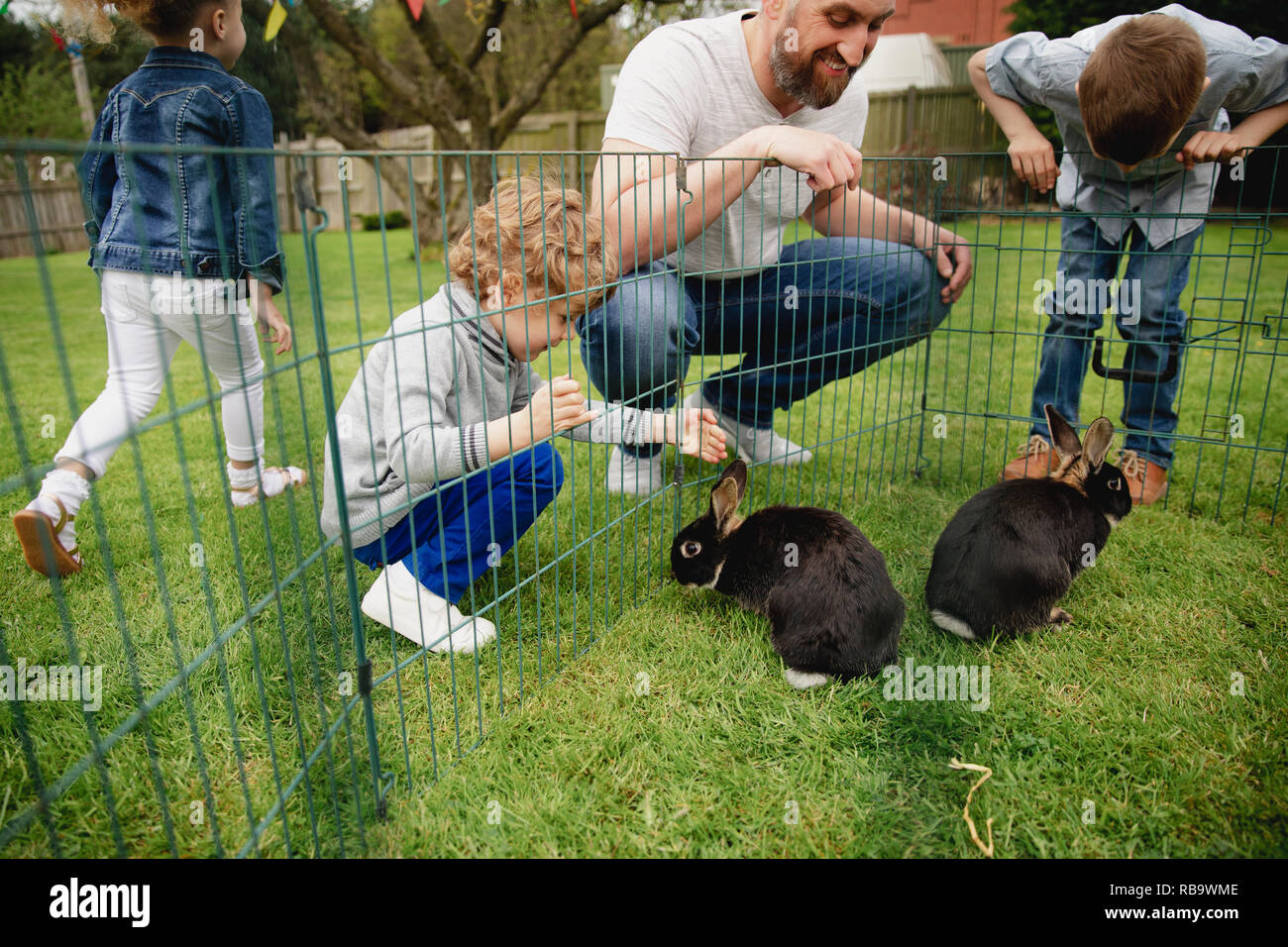 Group of children kneeling outdoors next to a rabbit pen. They are ...