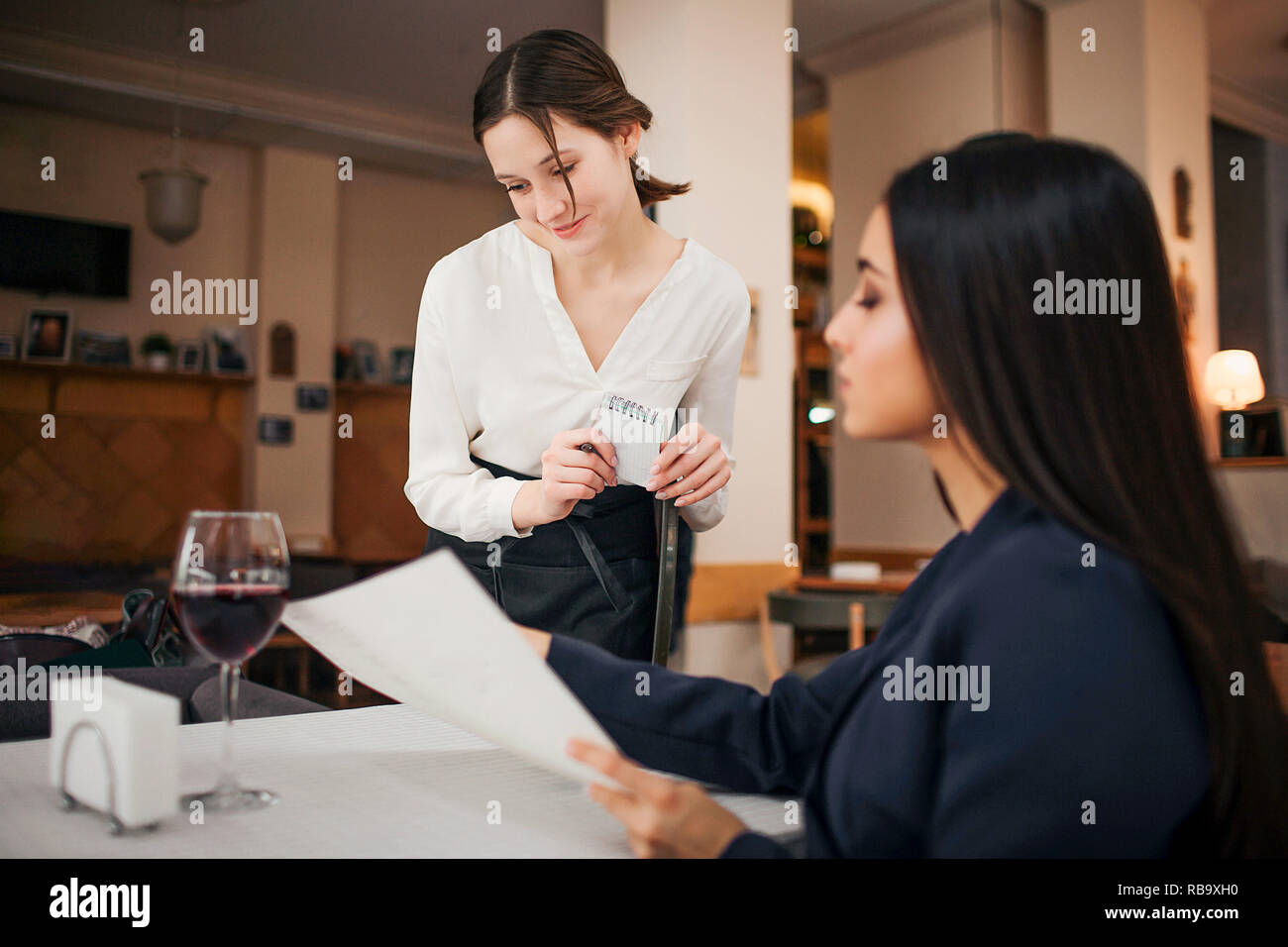 Young waitress stand besides sitting customer and look at menu she ...