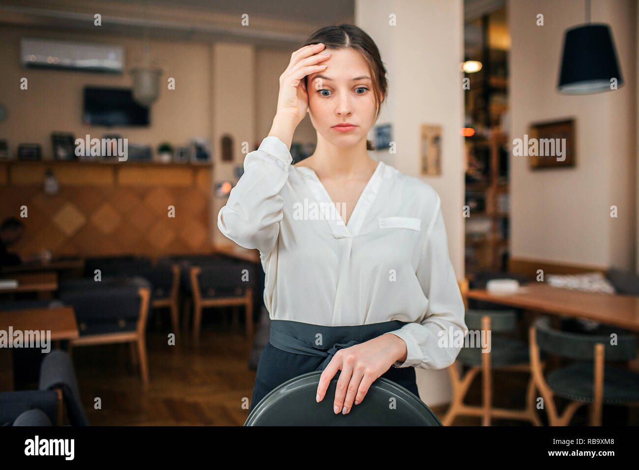 Frustrated young waitress look down. She hold tray in left hand. Right ...