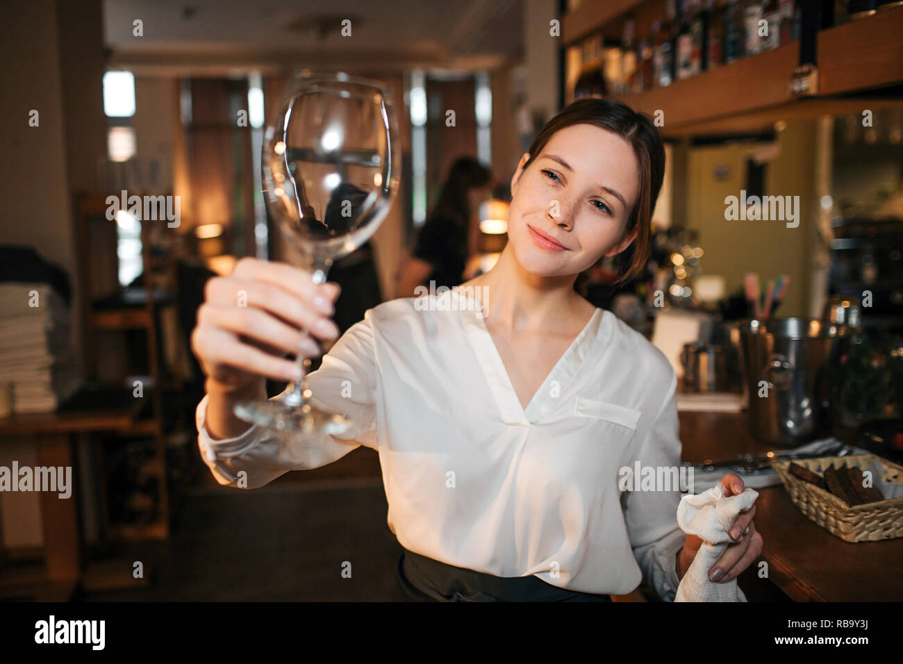 Picture of young waitress stand and look at clean glass for wine. She ...