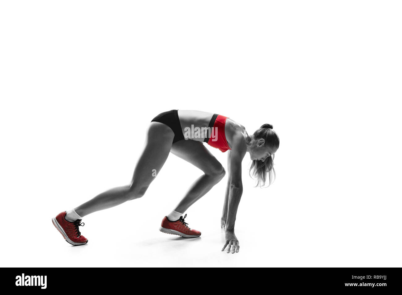 Portrait of young sporty woman at starting block of race isolated over ...