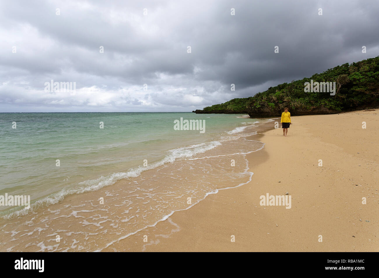 Young woman in yellow jacket standing, walking in shallow water on a ...