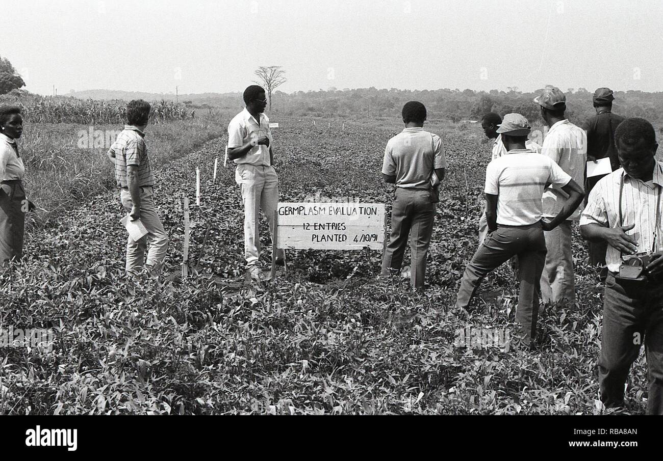MEN AND WOMAN STANDING IN A FIELD LOOKING AT CROPS. SIGN SAYS GERMPLASM ...