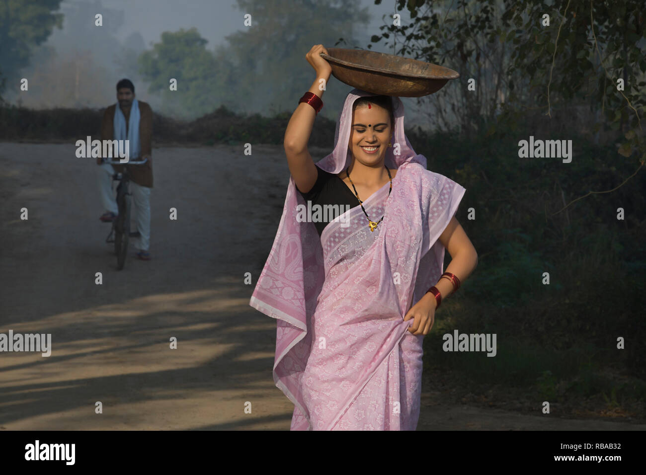Smiling rural woman going to work carrying an iron gold pan on her head ...
