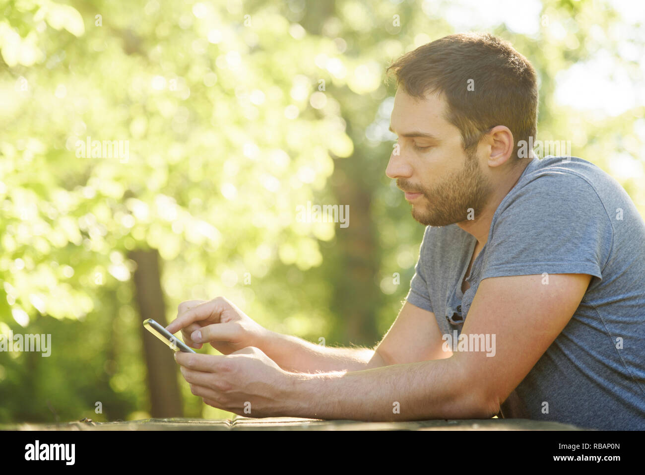 Young man sitting in park, relaxing and using mobile smart phone for ...
