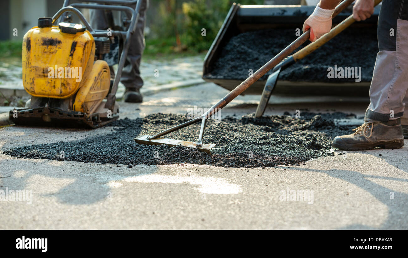 Low angle view of two workers arranging fresh asphalt mix with rakes ...