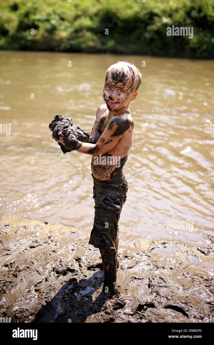 A happy young boy child is covered in mud as he laughs, swims, and ...
