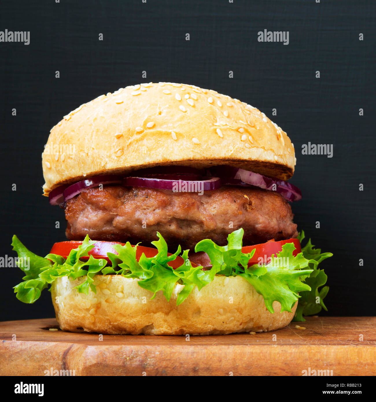 Fresh and delicious homemade burger on wooden board, side view. Close ...