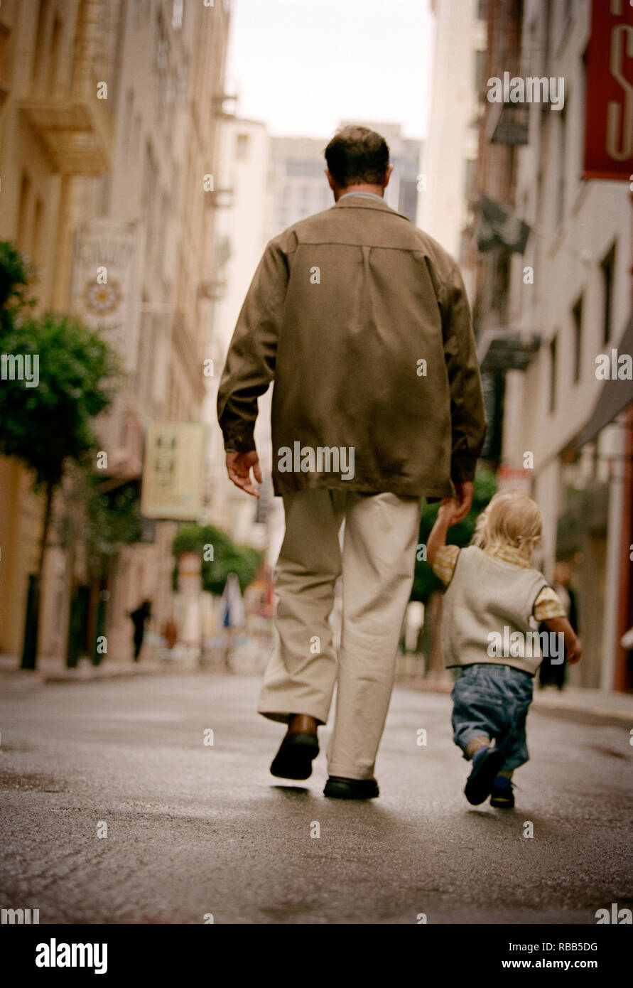 Man and child walking down city street holding hands Stock Photo - Alamy