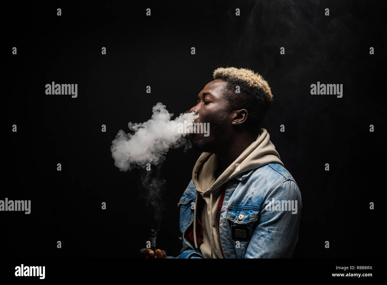 Side view portrait of guy holding vape device and exhaling cloud of ...