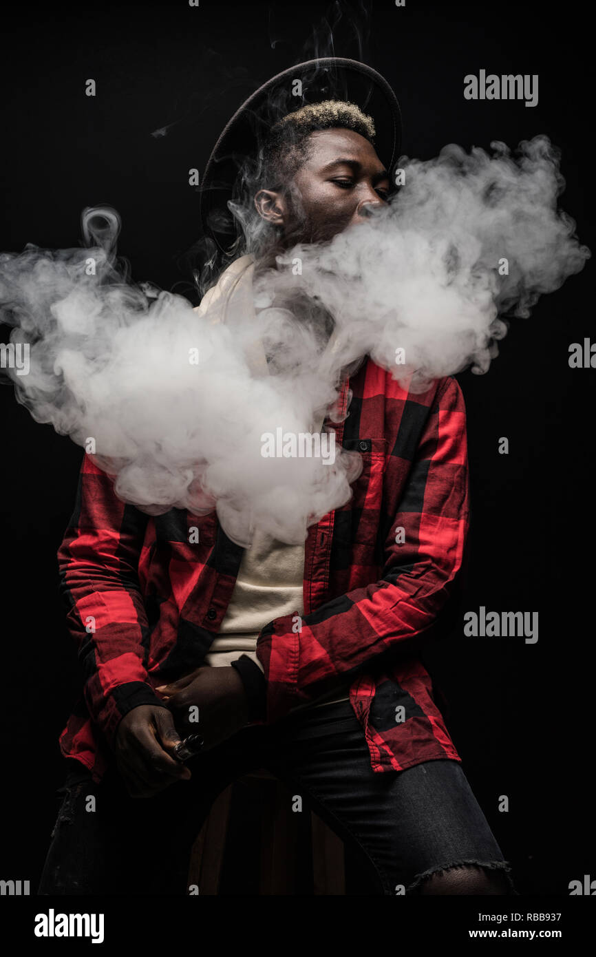 Young african man on a black background holding an electronic cigarette ...