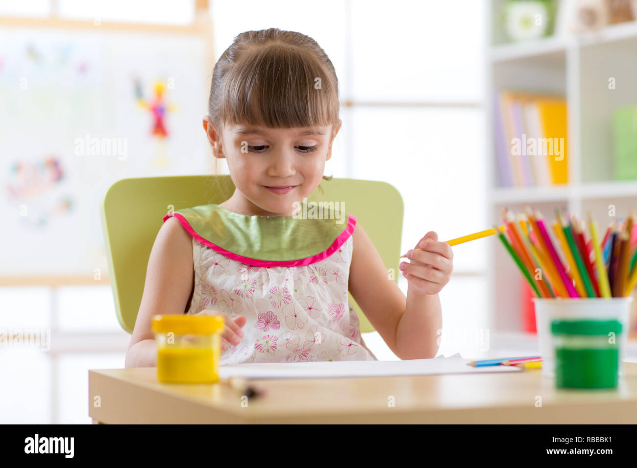 cute child girl cheerfully spending time using color pencils while ...