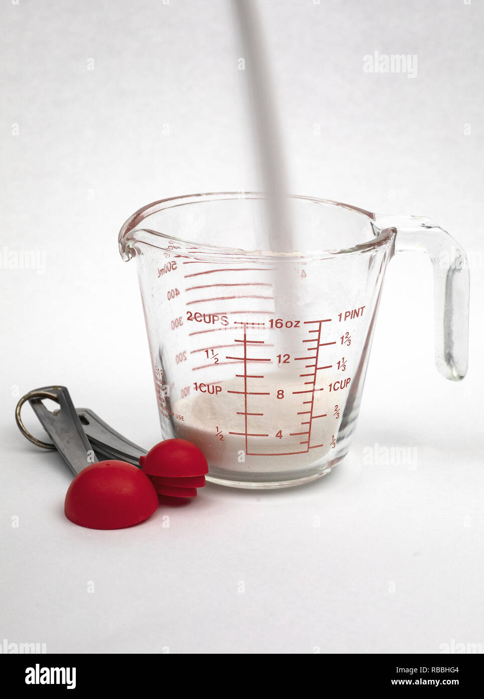 Pouring white cane sugar into a measuring cup with measuring spoons in ...