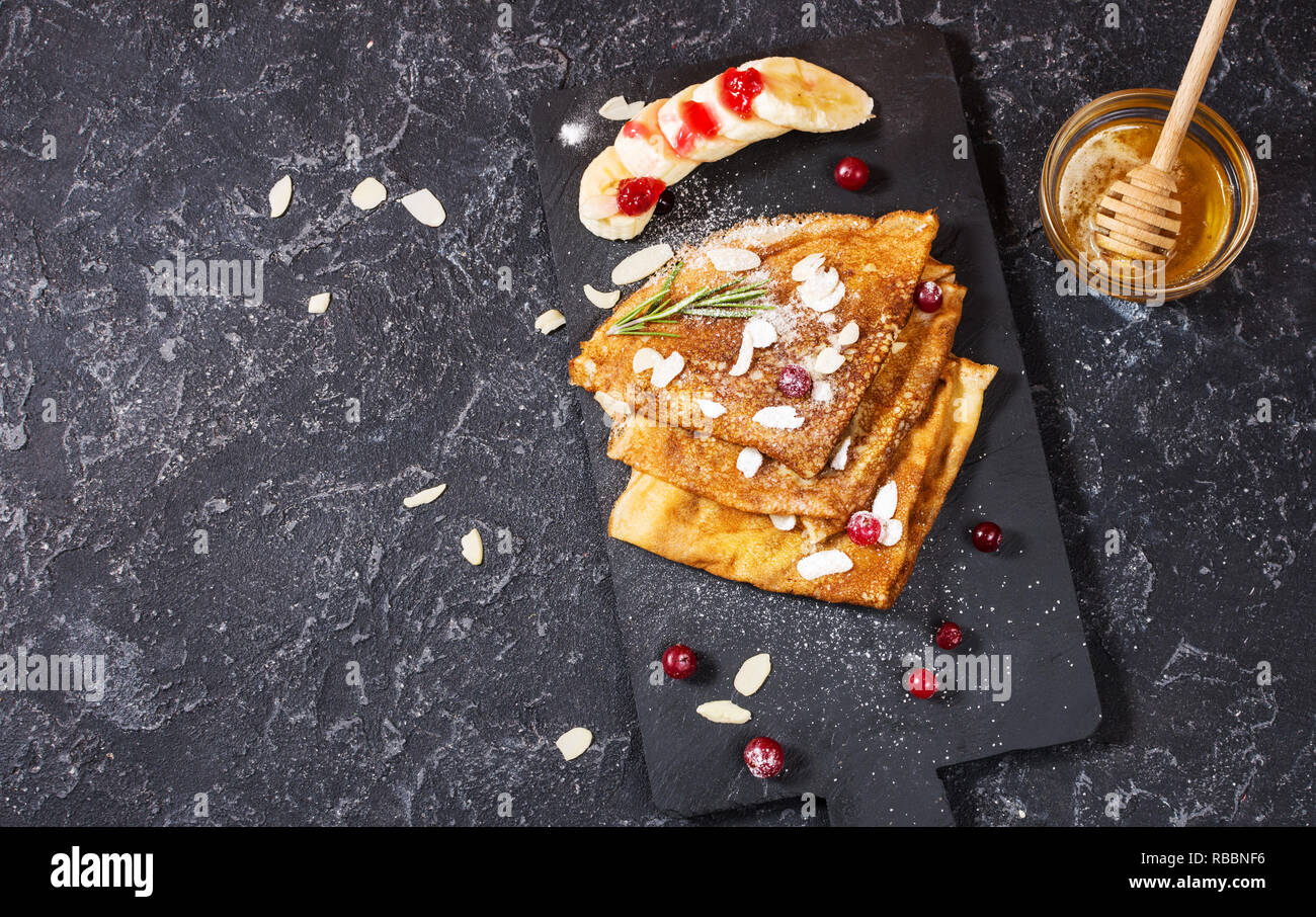 Traditional crepes with banana and berries on black stone background ...