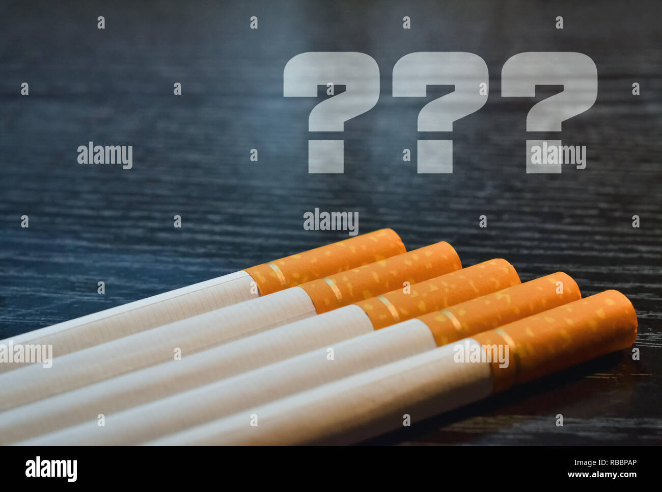 Closeup of five cigarettes and three question marks on dark background ...