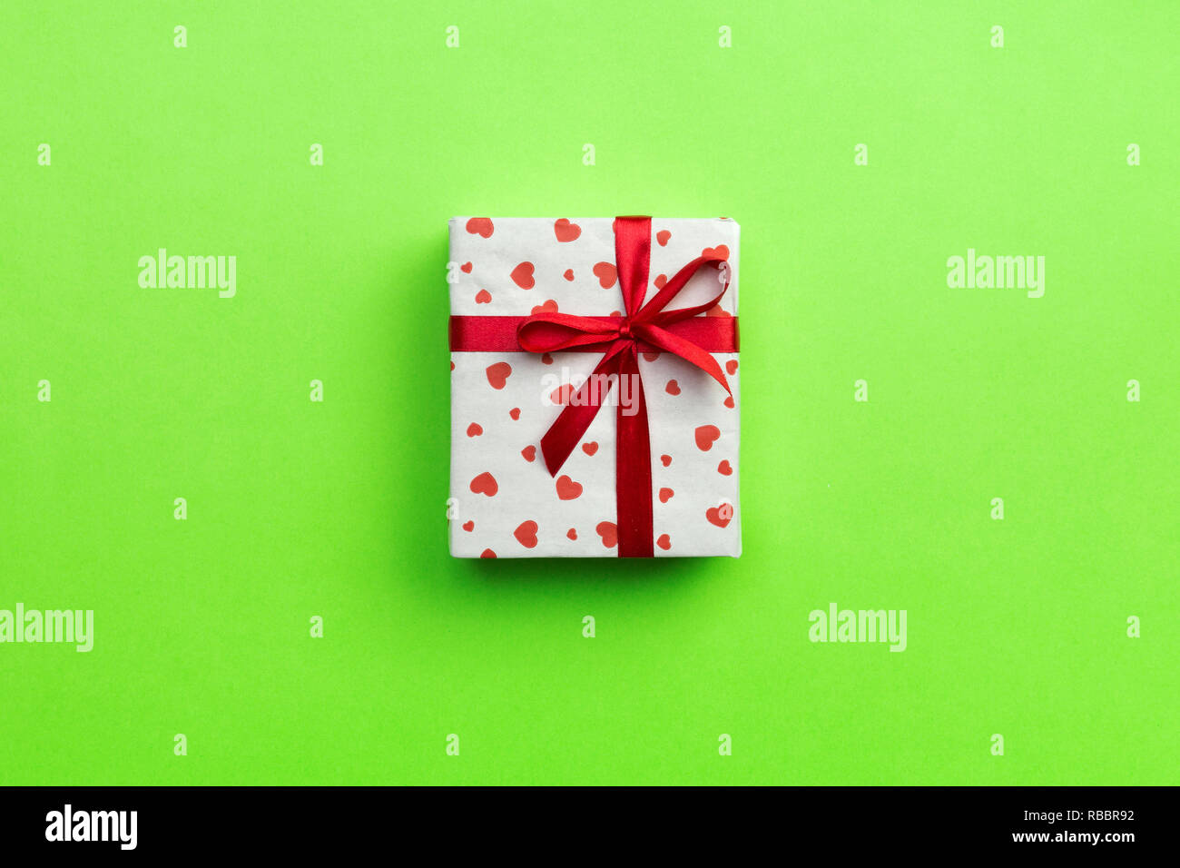 Gift box with red ribbon and heart on green background, top view with ...