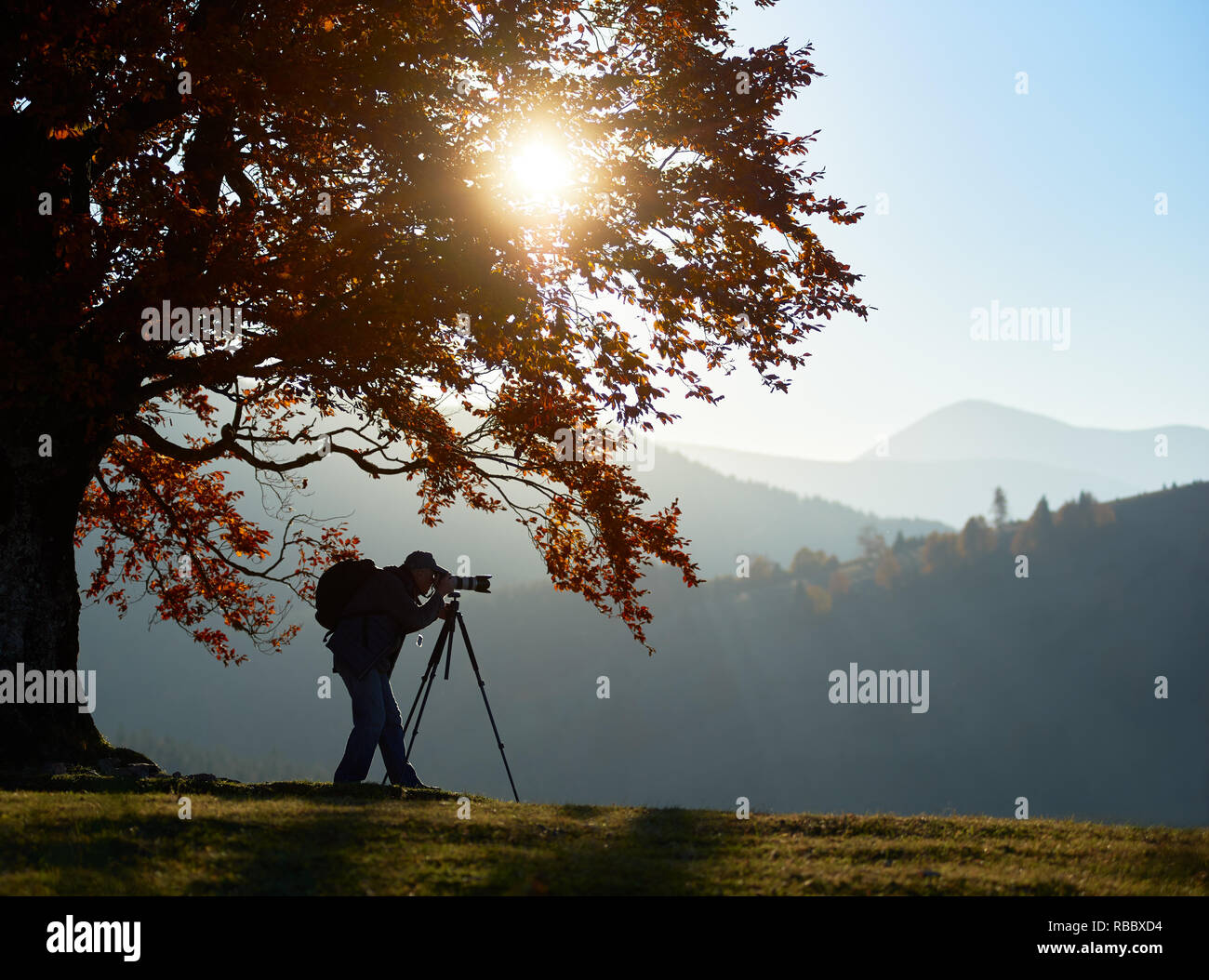 Tourist photographer with backpack using tripod and professional camera ...
