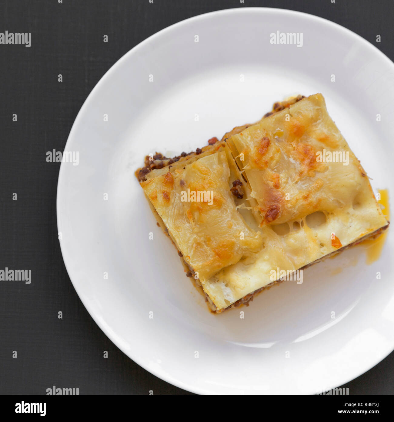 Traditional beef lasagne on a white round plate over black background ...