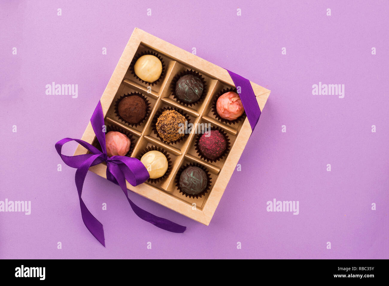 A set of assorted chocolates in a paper box with a satin purple ribbon ...