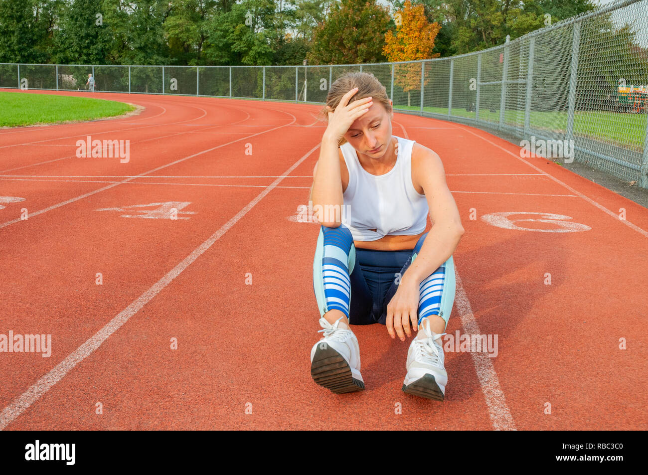 Tired woman runner taking a rest after run sitting on the running track ...
