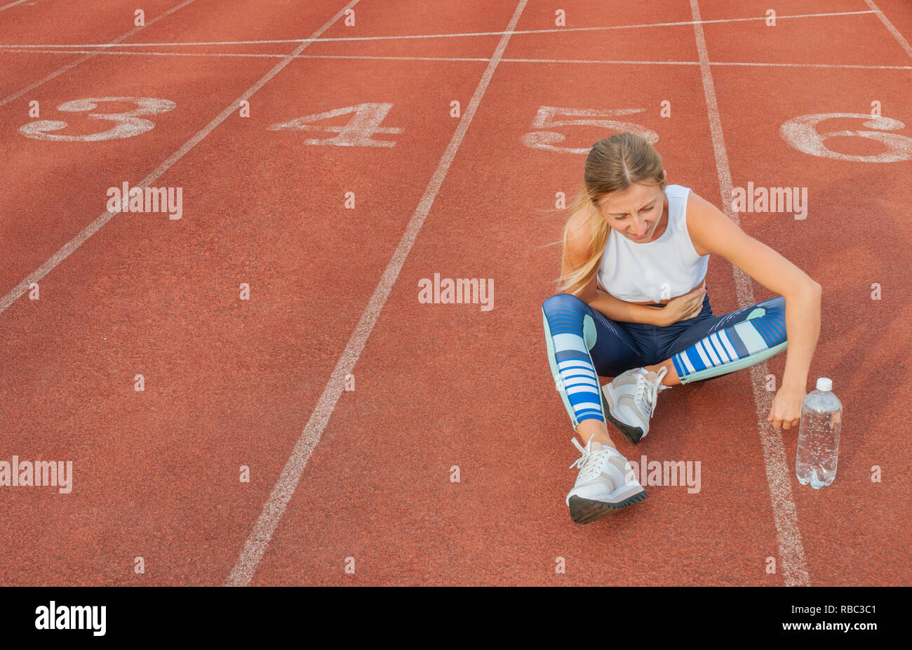 Tired woman runner taking a rest after run sitting on the running track ...