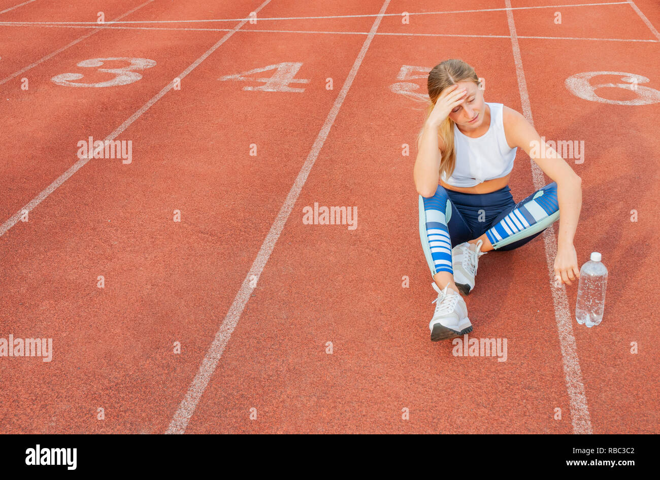 Tired woman runner taking a rest after run sitting on the running track ...