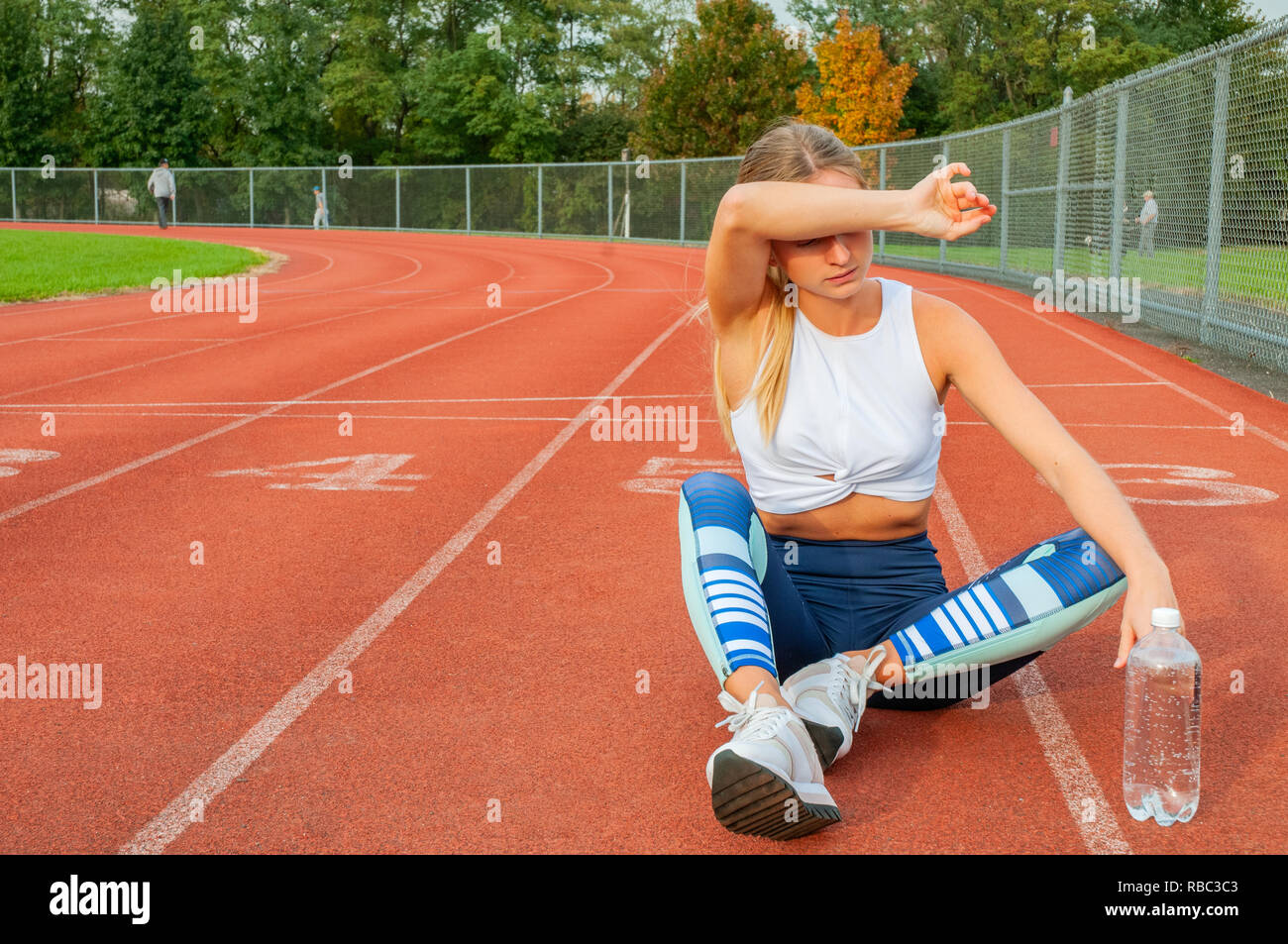 Tired woman runner taking a rest after run sitting on the running track ...