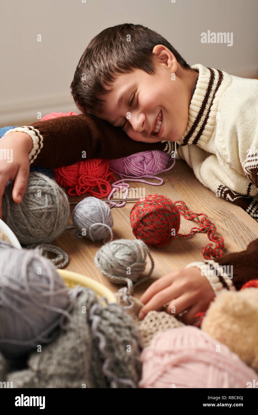 Child boy is learning to knit. He is dreaming and closing eyes ...