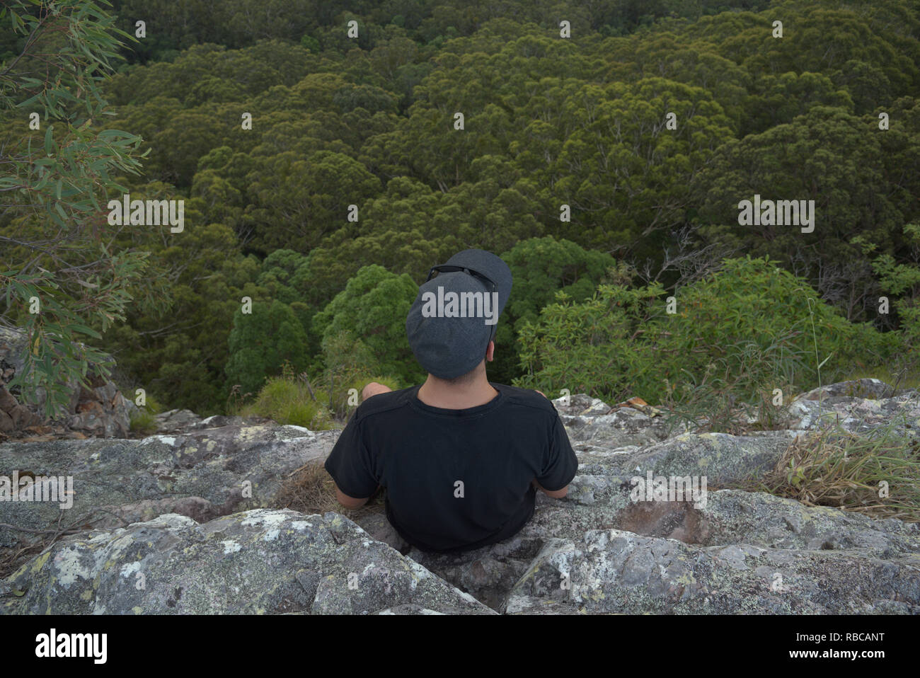 Man sitting on the edge of a cliff on top of a forest Stock Photo - Alamy