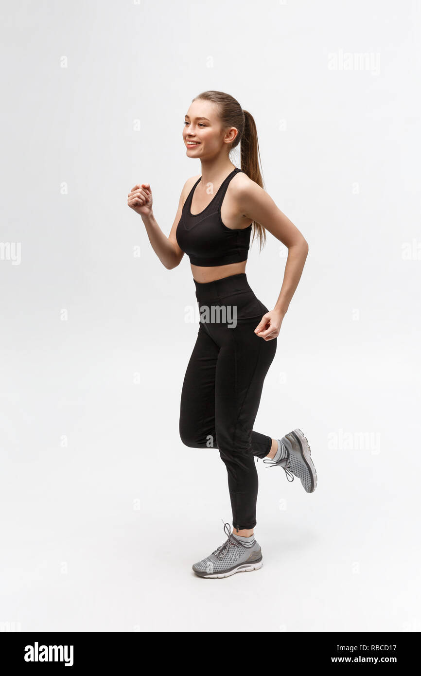 Full length picture of a sports woman running in studio over gray ...