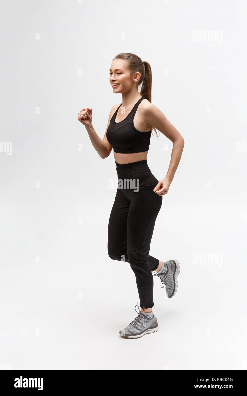 Full length picture of a sports woman running in studio over gray ...