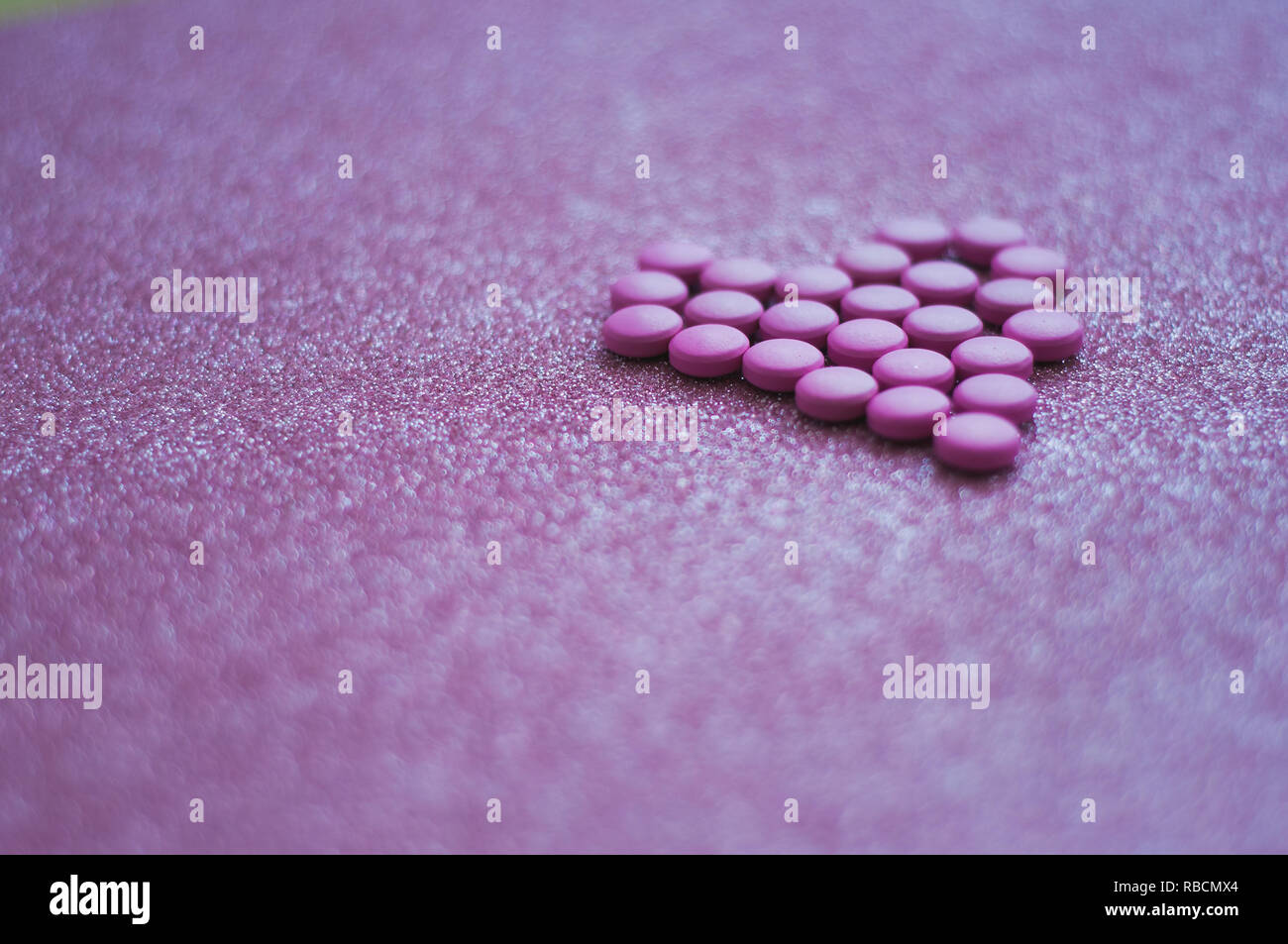 pink pills laid out in shape of a heart on glitter pink background ...