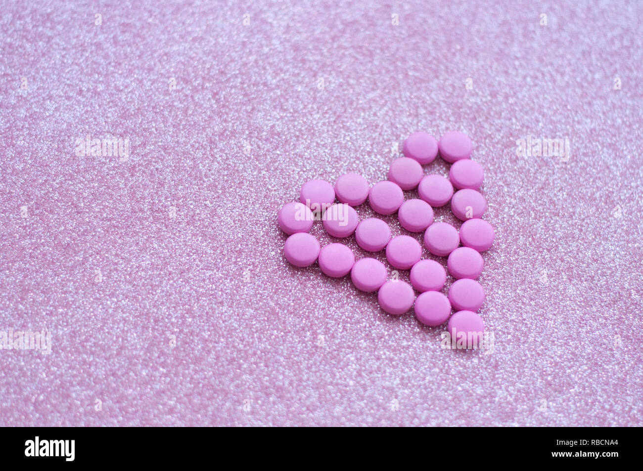 pink pills laid out in shape of a heart on glitter pink background ...