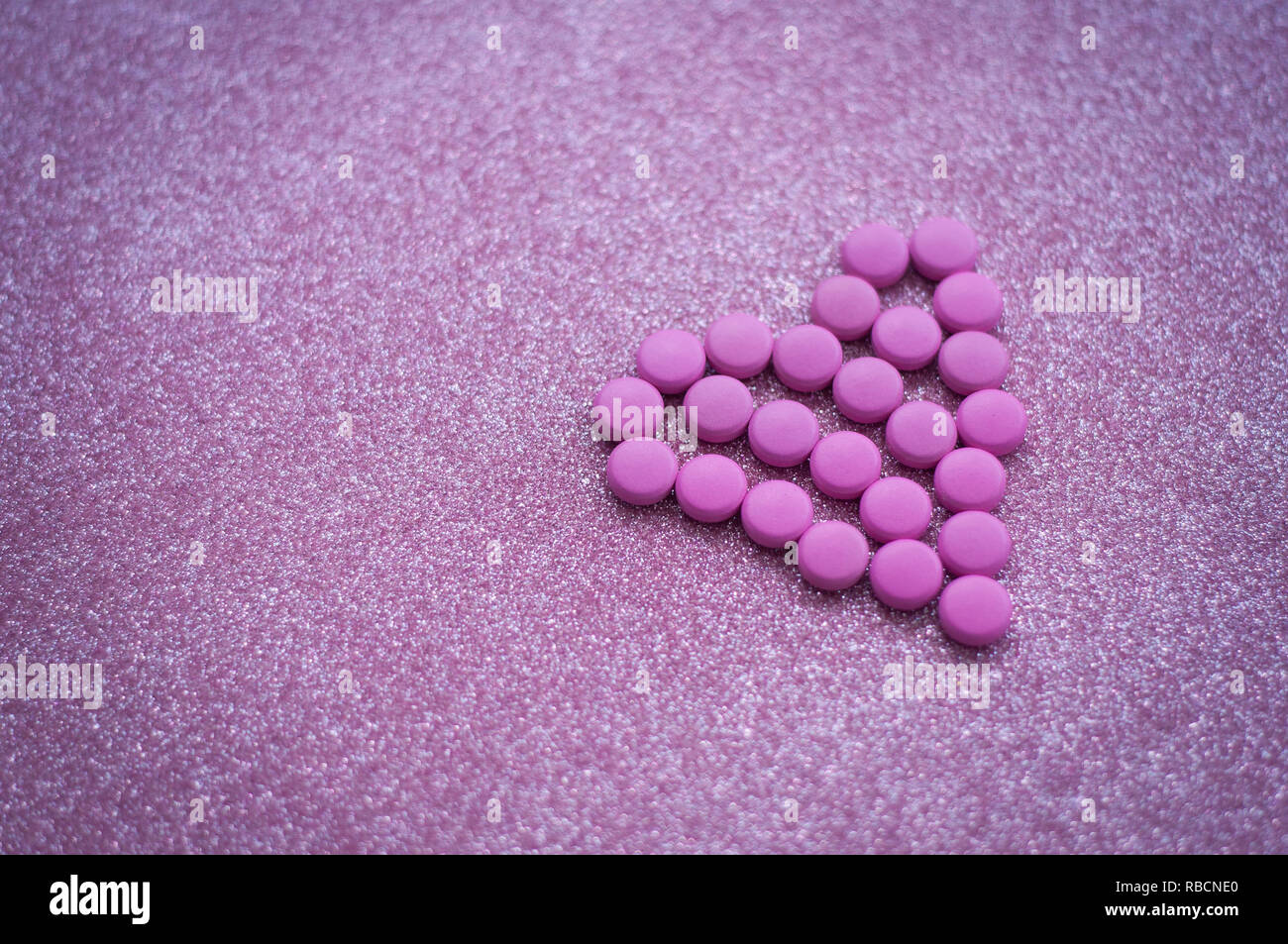 pink pills laid out in shape of a heart on glitter pink background ...