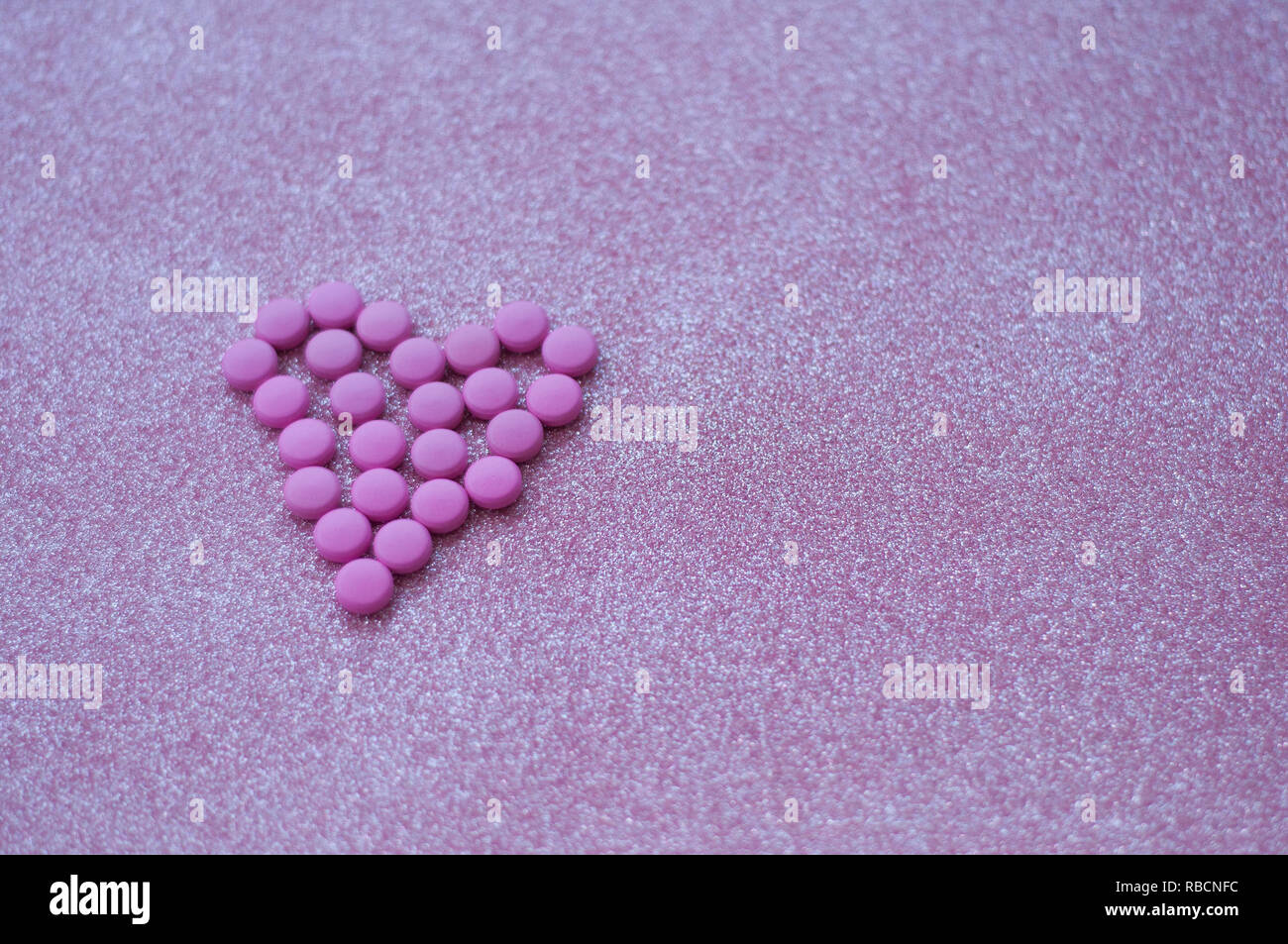 pink pills laid out in shape of a heart on glitter pink background ...