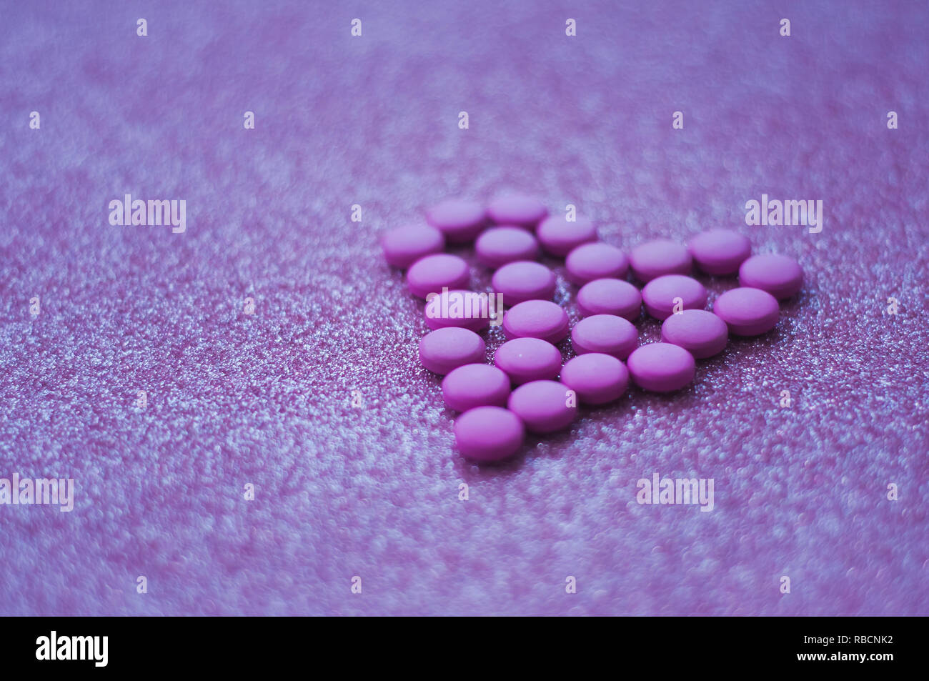 pink pills laid out in shape of a heart on glitter pink background ...