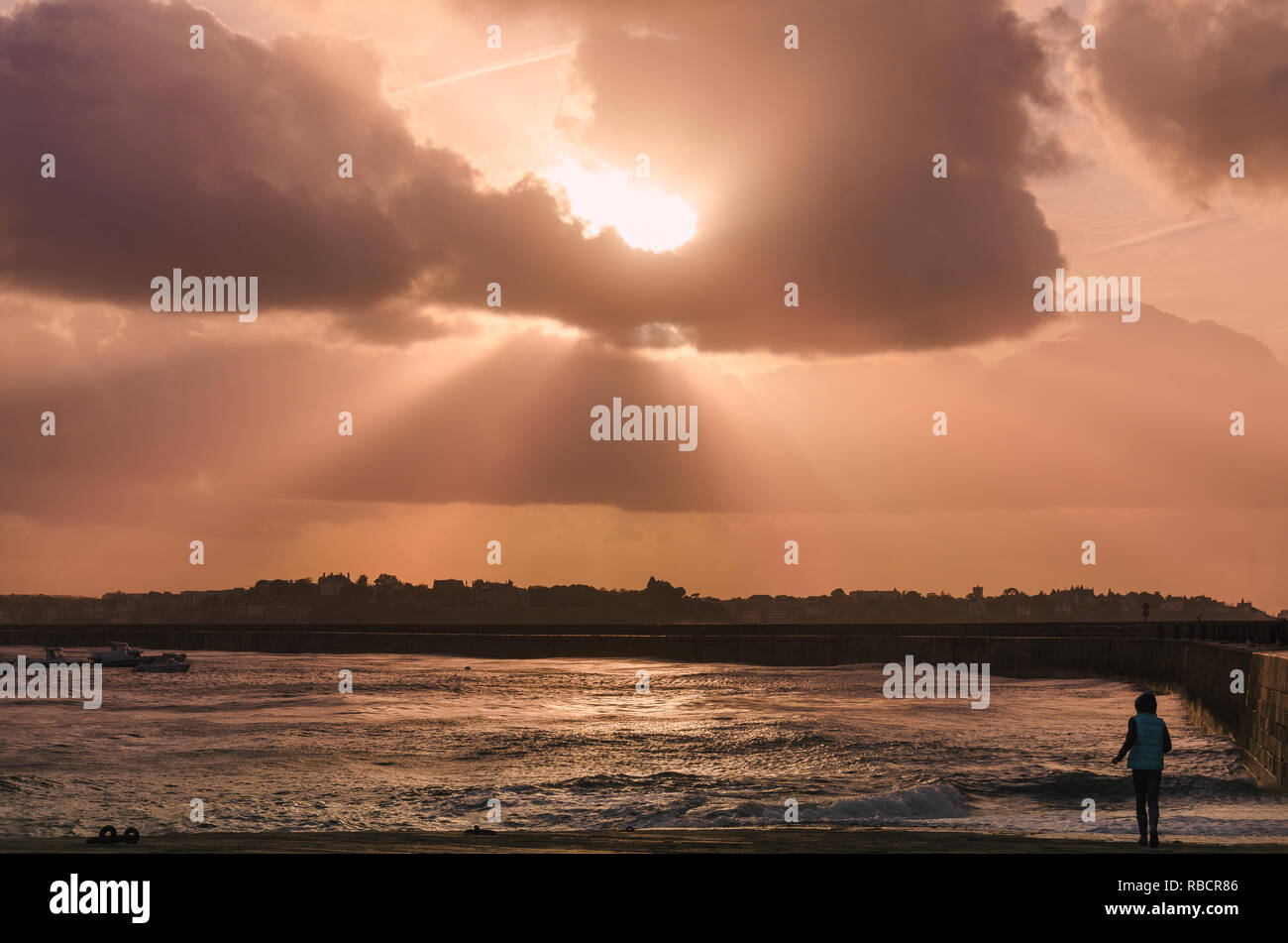 Sunset on a city harbour, with a peer and sun rays breaking through the ...