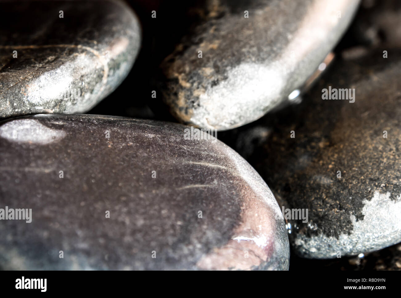 Glossy surface of round black stone on ground beside the waterfall ...