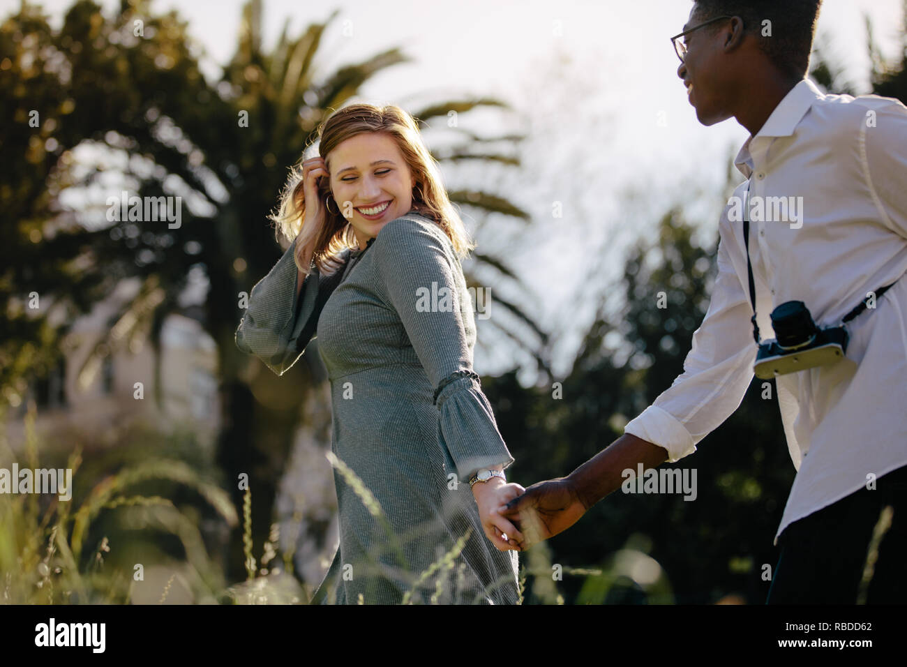 Smiling Man And Woman Walking In Park Holding Hands Interracial Couple