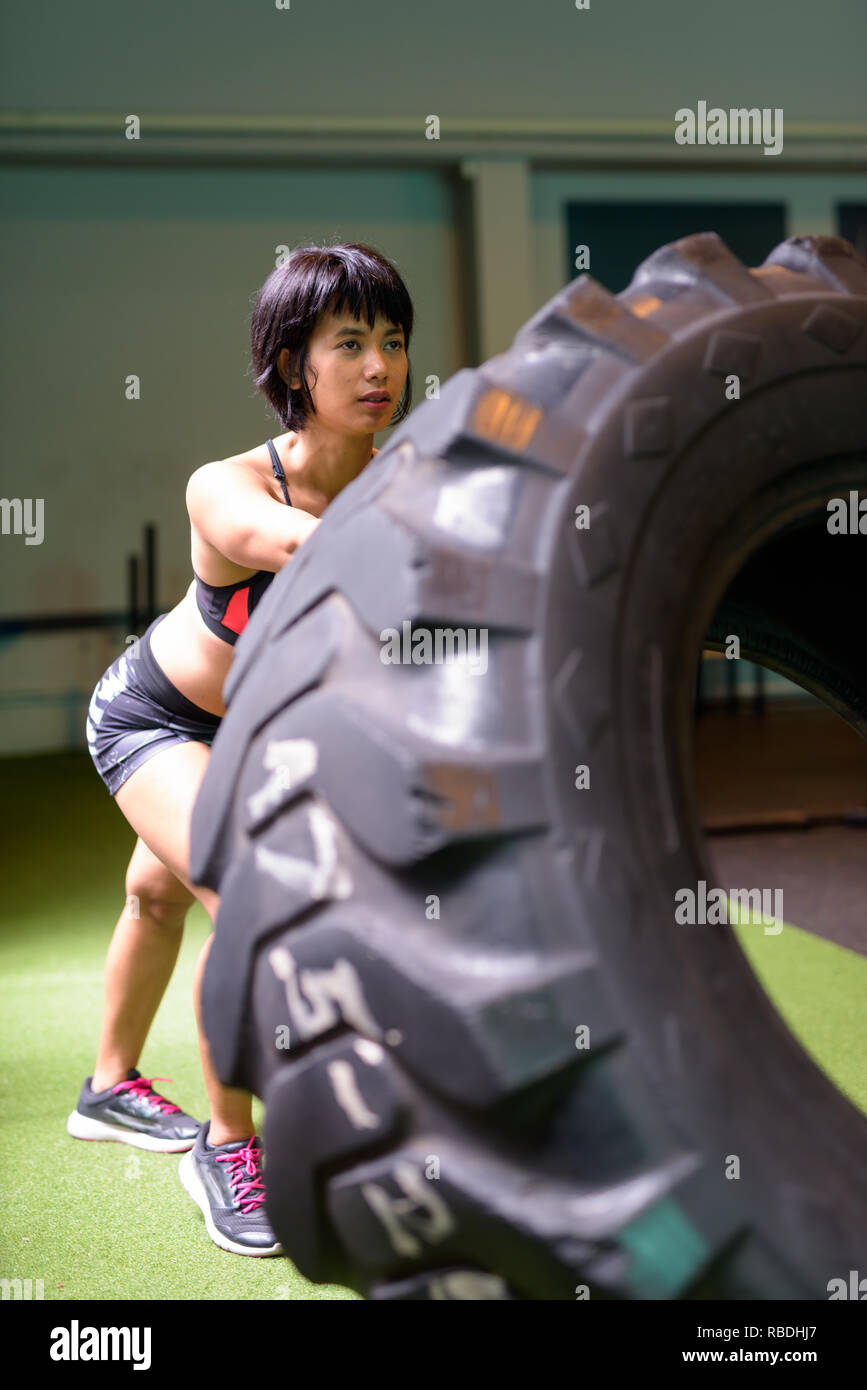 Asian fitness woman pushing and flipping wheel truck tire at gym Stock ...