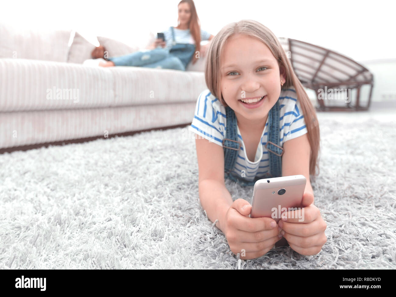 cute little girl with smartphone lying on the carpet in the living room ...
