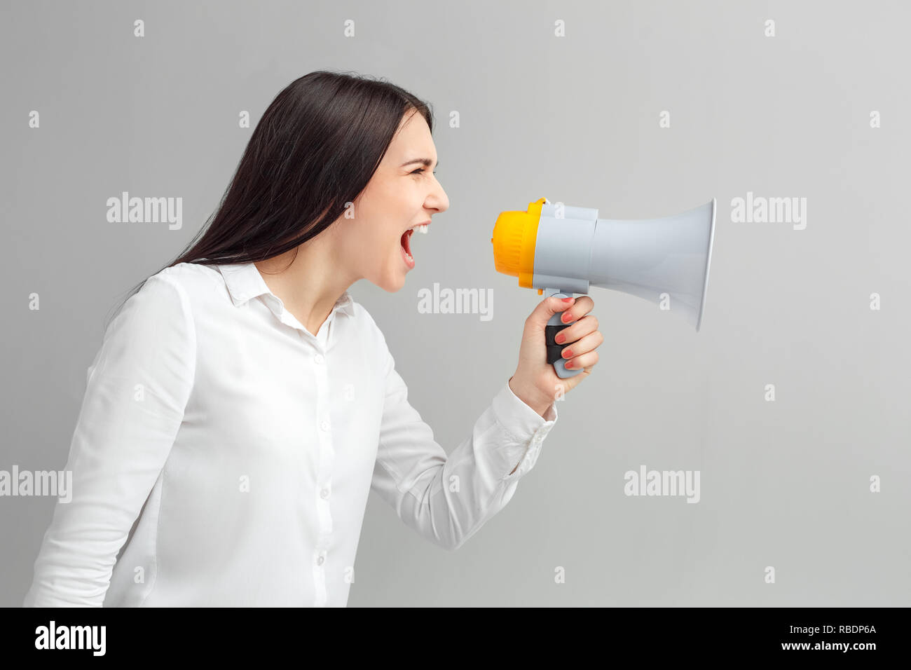 Young woman studio standing isolated on gray wall shouting at megaphone ...